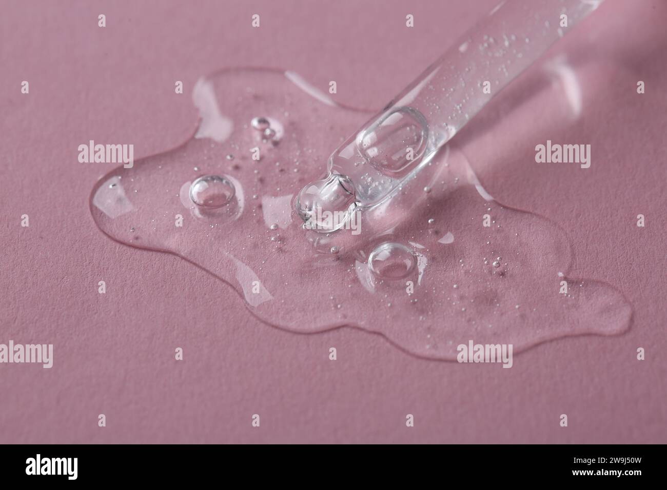 Dripping cosmetic serum from pipette onto pink background, macro view ...