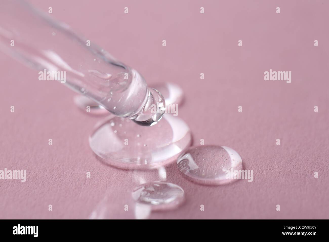 Dripping cosmetic serum from pipette onto pink background, macro view ...