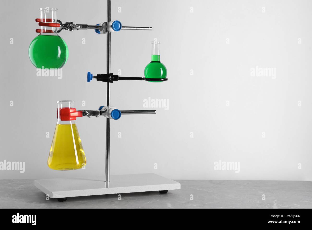 Retort stand and laboratory flasks with liquids on grey table against ...