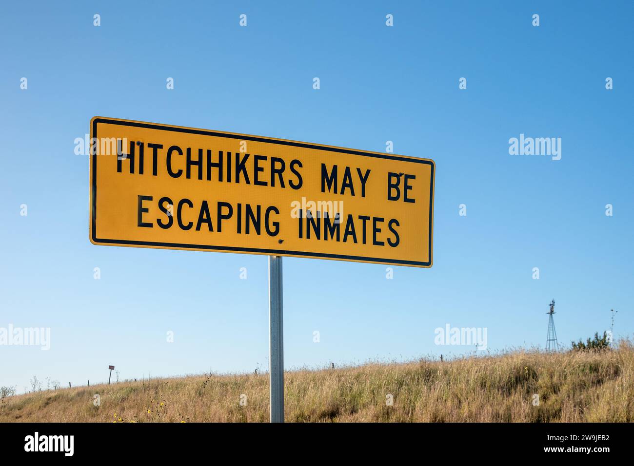 Large yellow roadside caution sign warns drivers Hitchikers May be ...