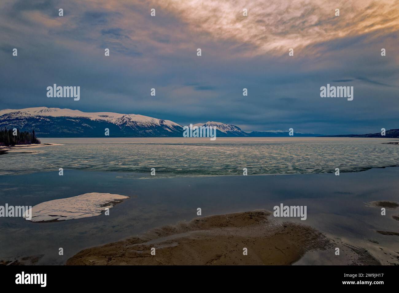 Drone image, view of the icy Atlin Lake, snowy mountain scenery behind ...