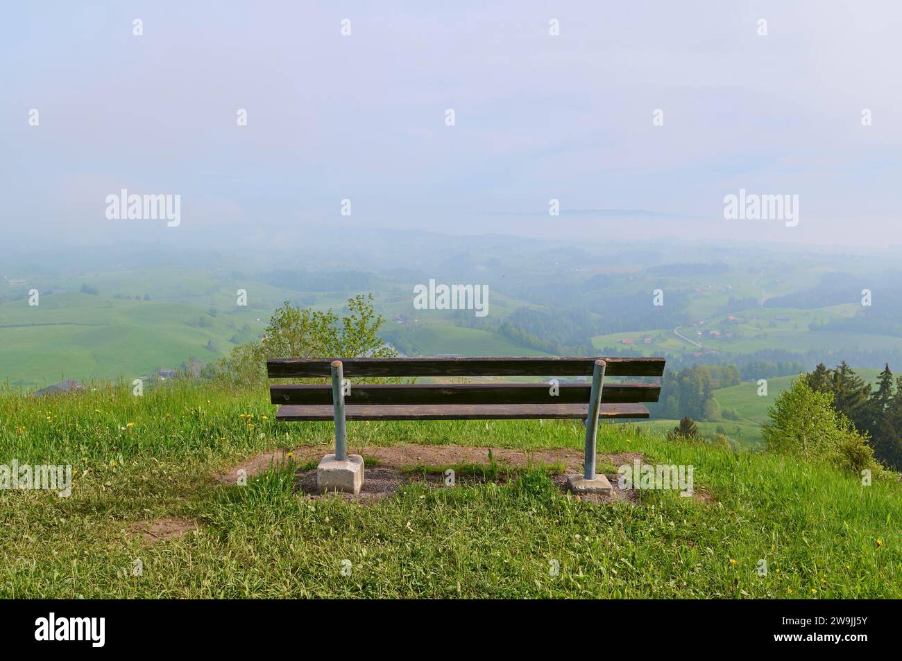 An empty bench stands in a meadow with a view of the mist-covered hills ...