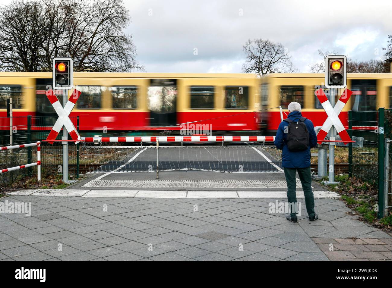 A man waits at a level crossing with a barrier while an S-Bahn train ...