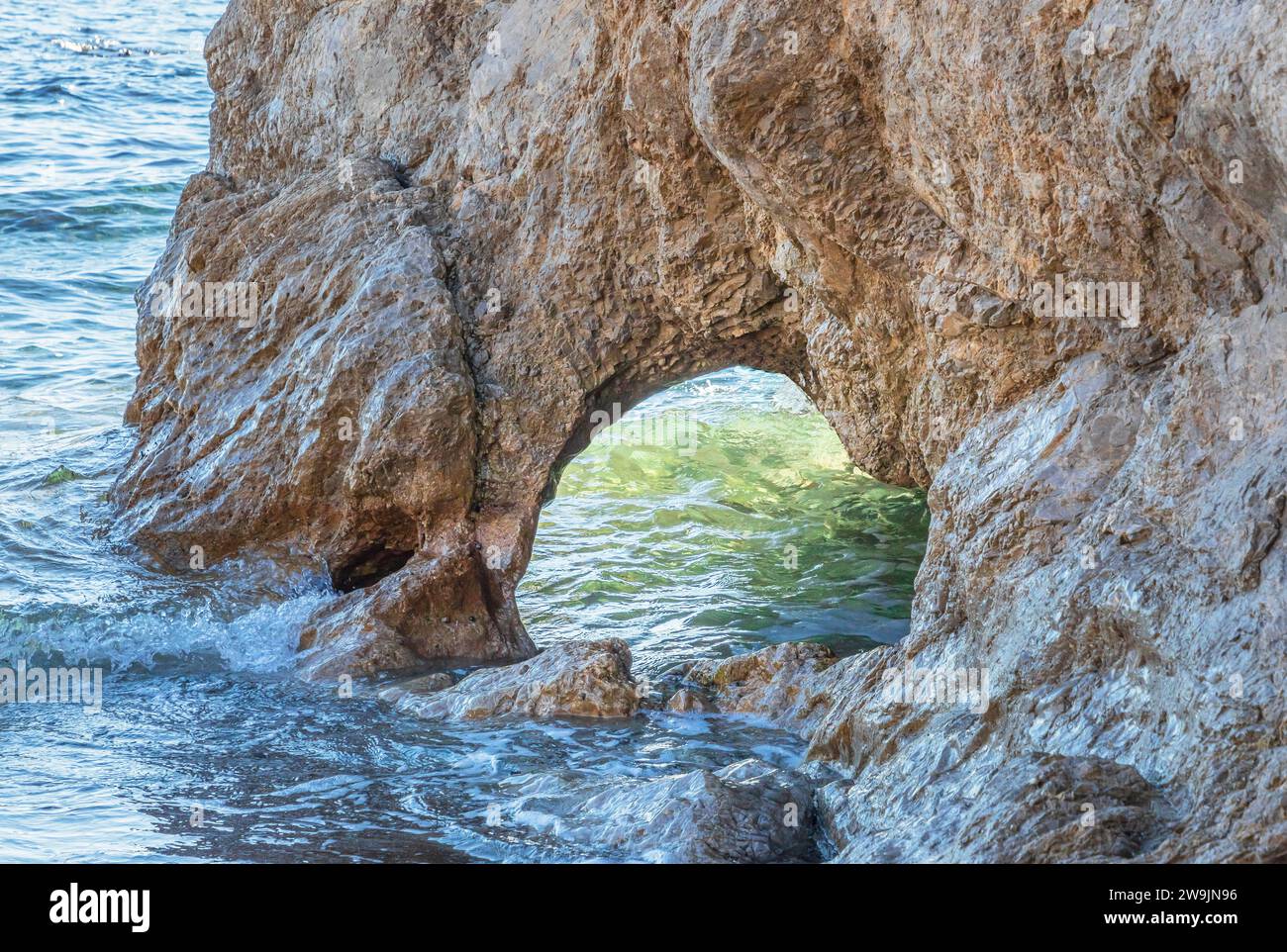 Archway in a rock formation on the shoreline with the sea coming in ...