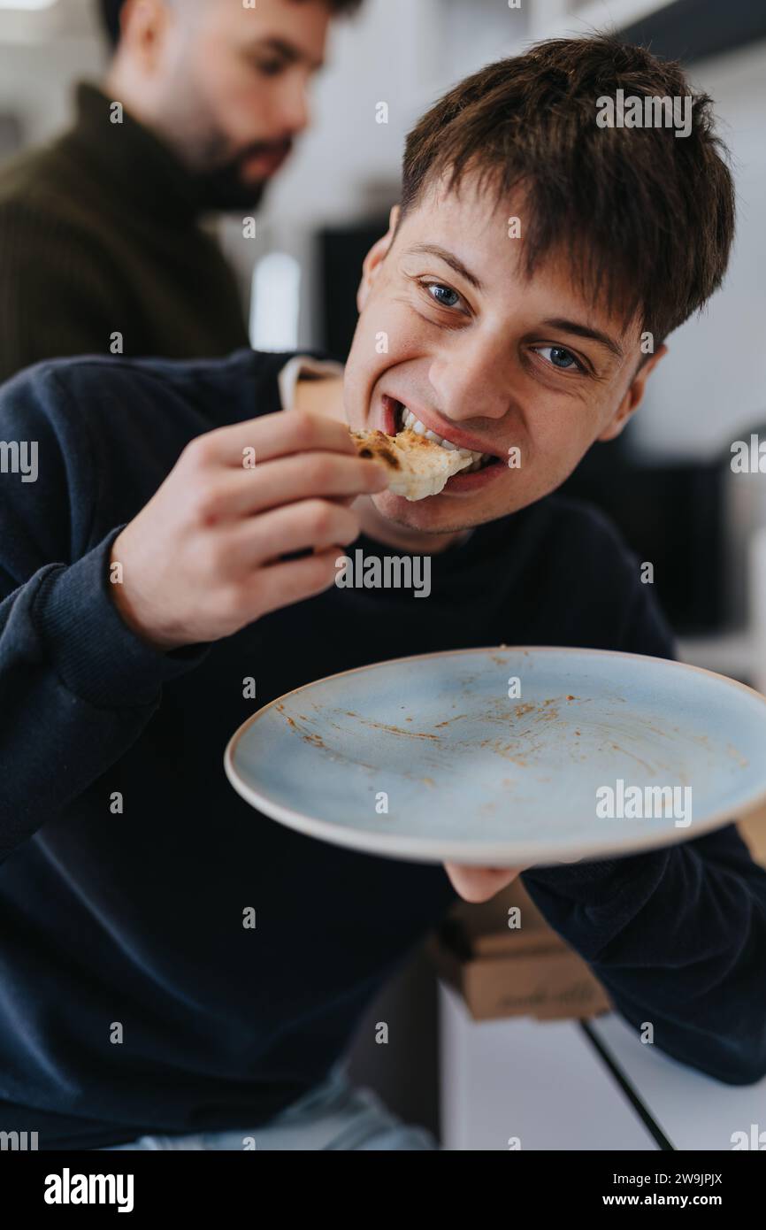 Handsome male person biting a tasteful slice of pizza while looking at ...