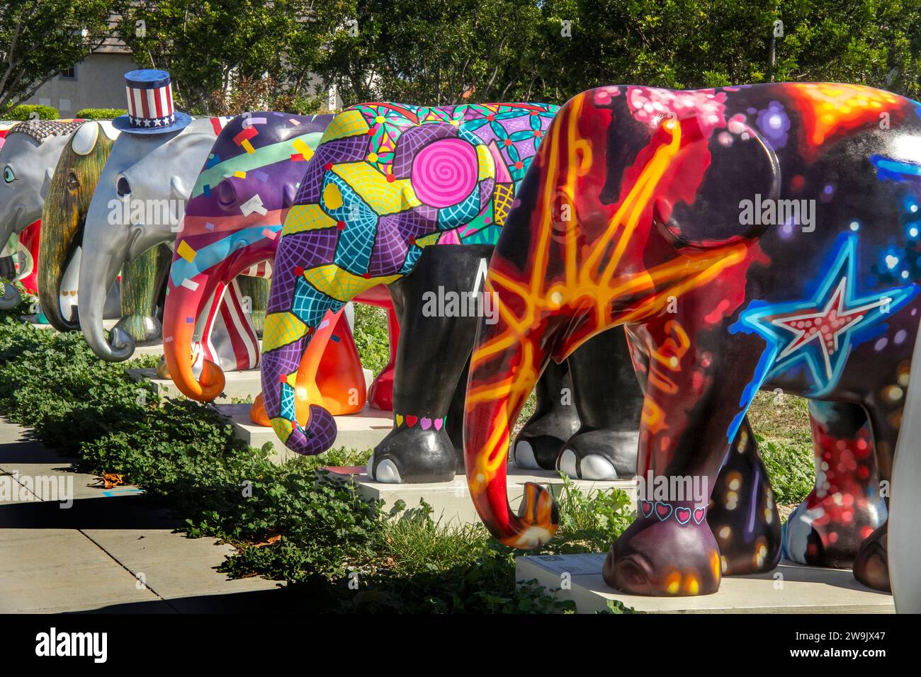 An exhibit of artistically painted elephants decorates a sidewalk in ...
