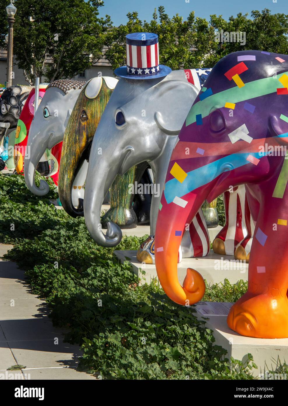 An exhibit of artistically painted elephants decorates a sidewalk in ...