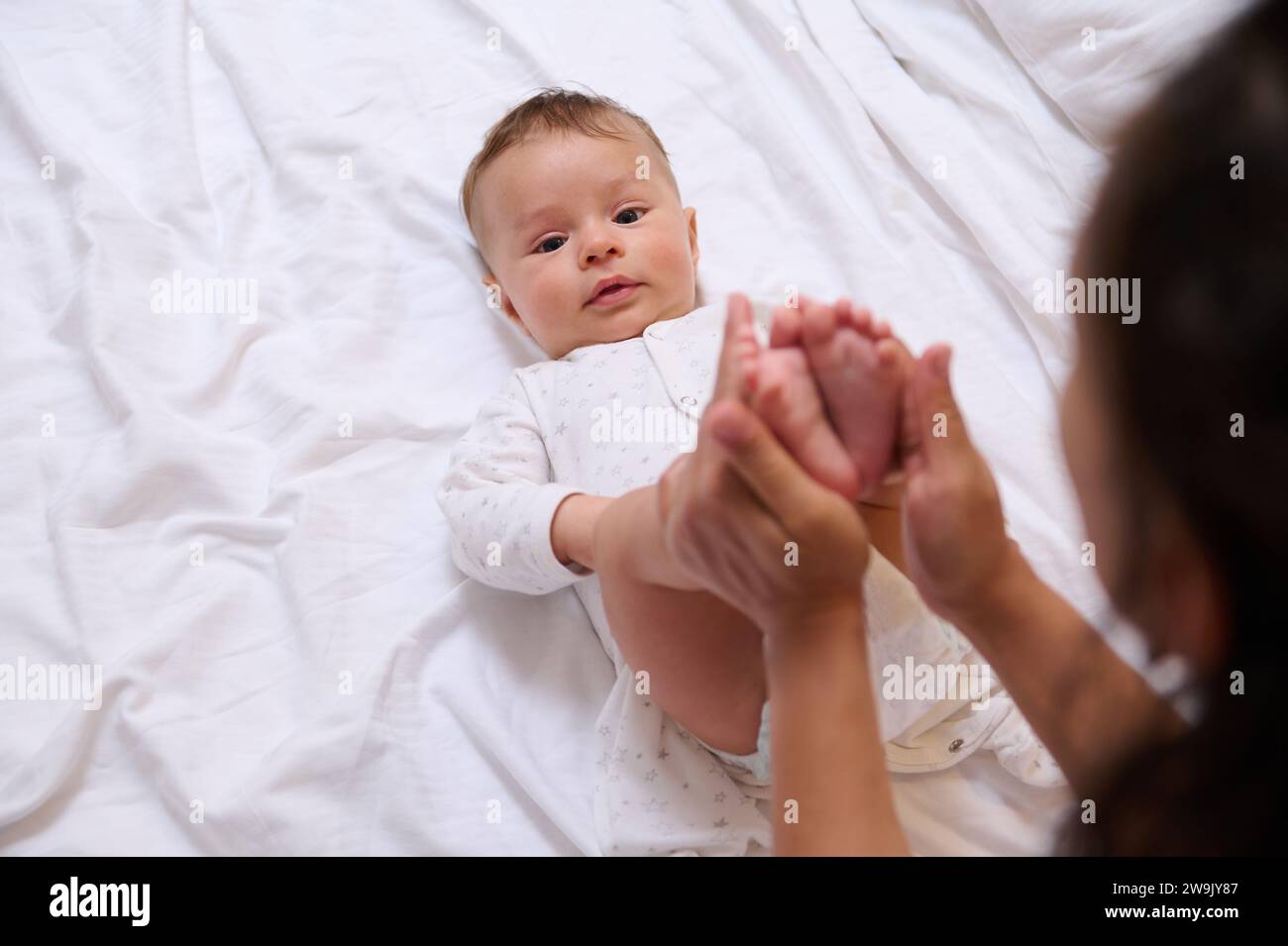 Beautiful newborn baby boy, looks at the camera while his loving caring young adult mother ...