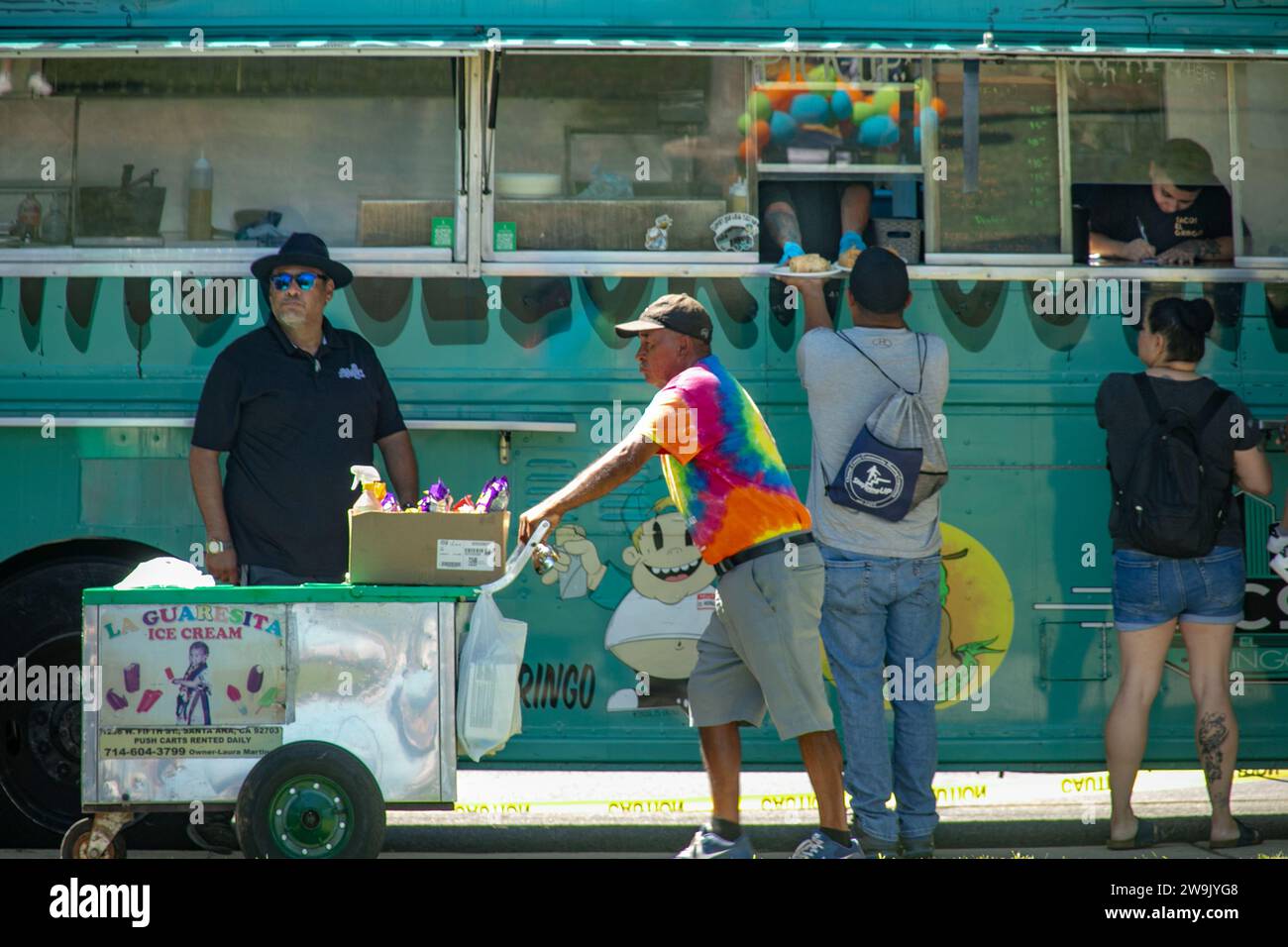 An ice cream vendor manages his push cart as a taco truck serves ...