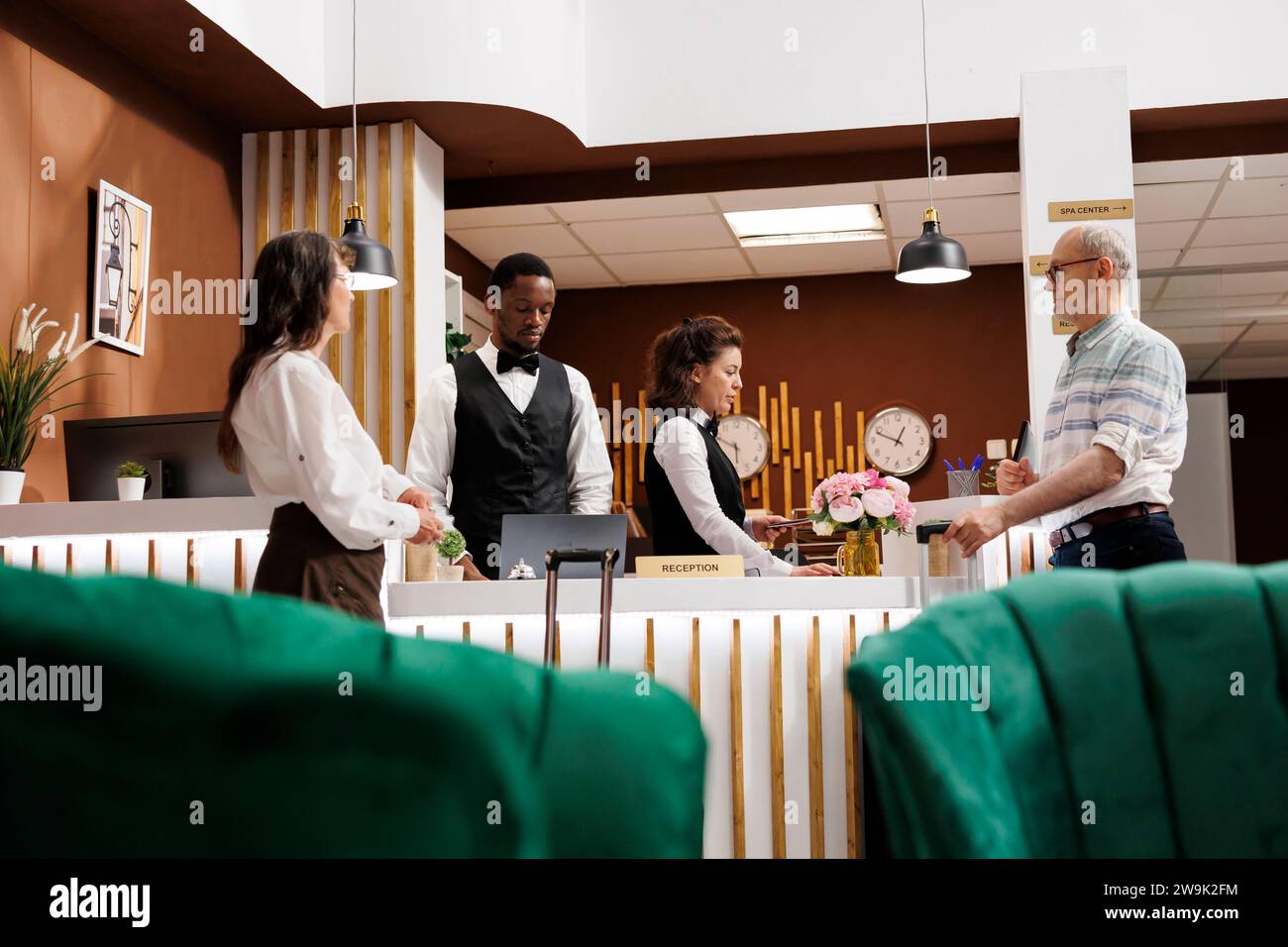Multiethnic employees welcome elderly guests at hotel reception with ...