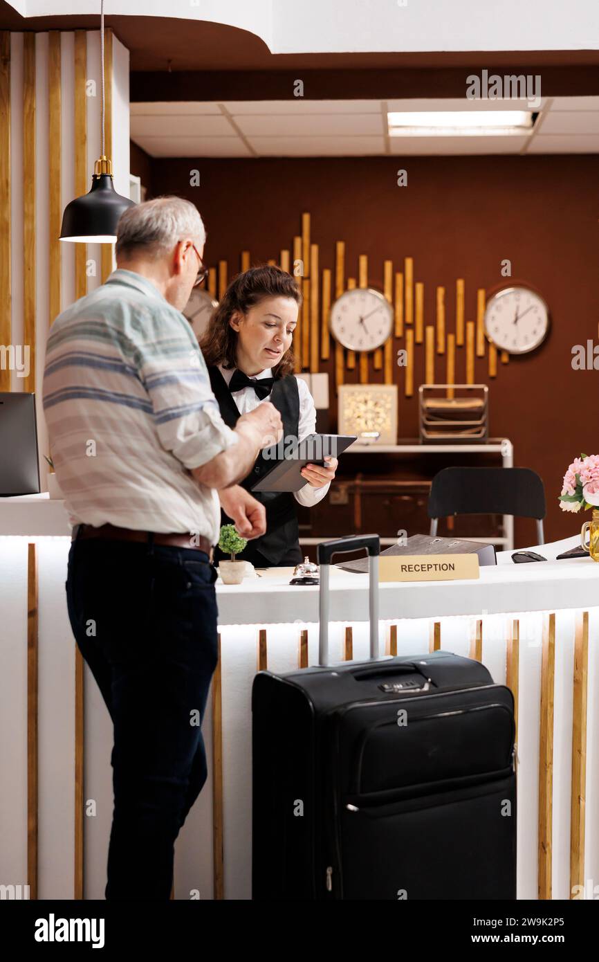 Elderly male traveller checks in at registration counter of hotel lobby ...