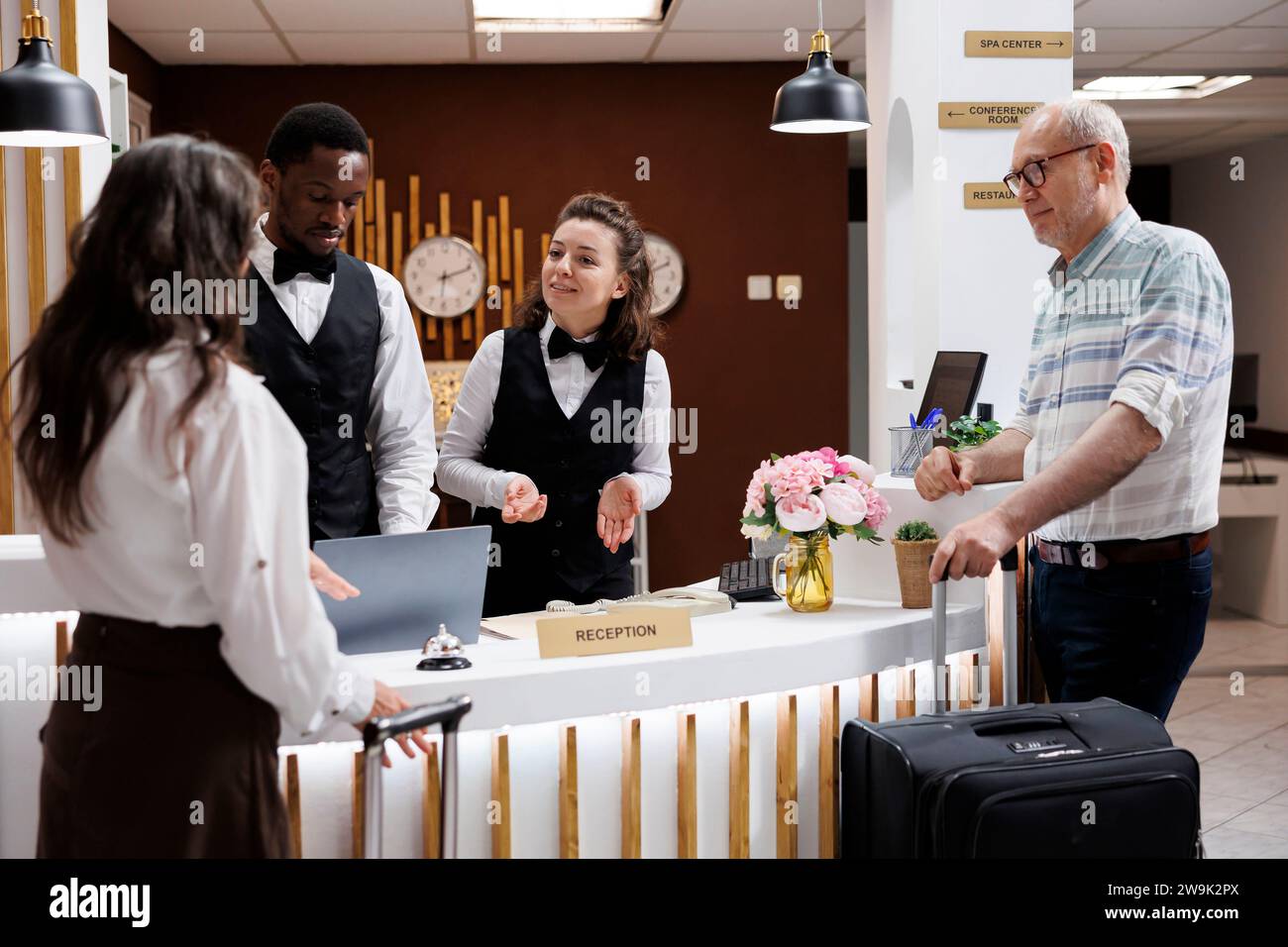 Assisting elderly guests at upscale hotel reception, concierge welcomes ...
