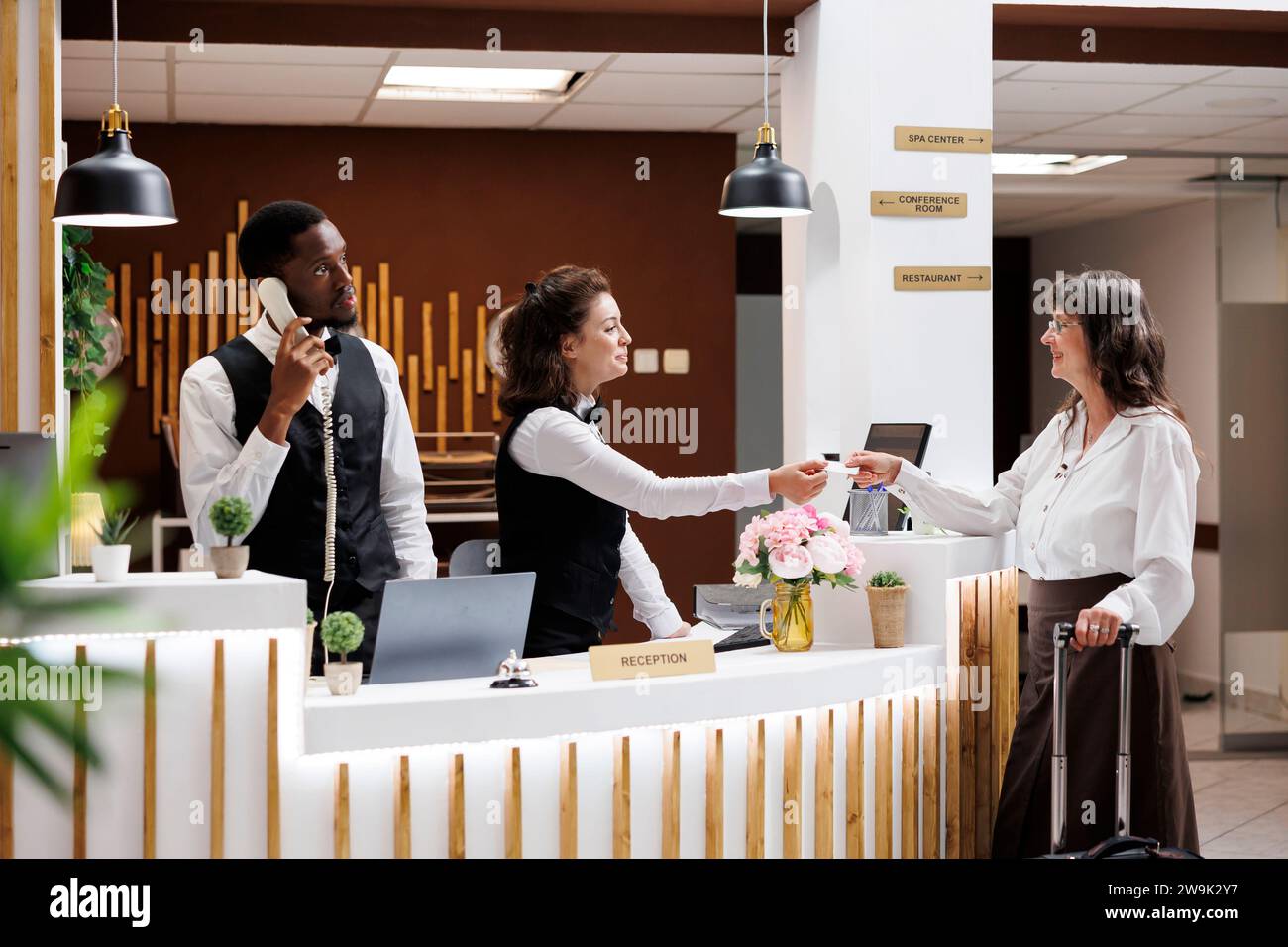 Retired senior woman taking key card from front desk staff and receiving access to accommodation ...