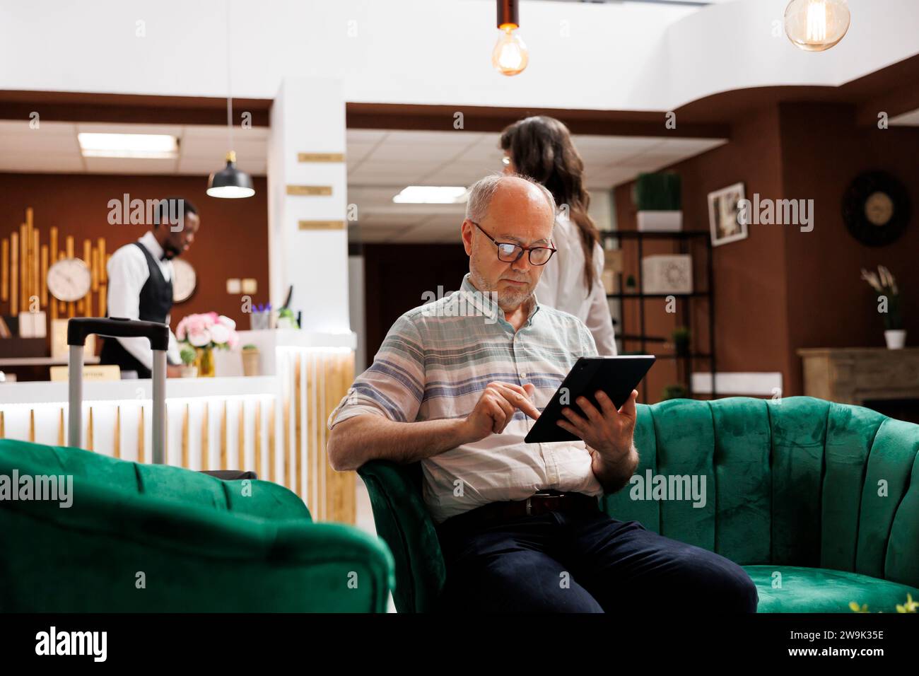 Elderly male tourist on lounge area couch, surfing the net on digital ...