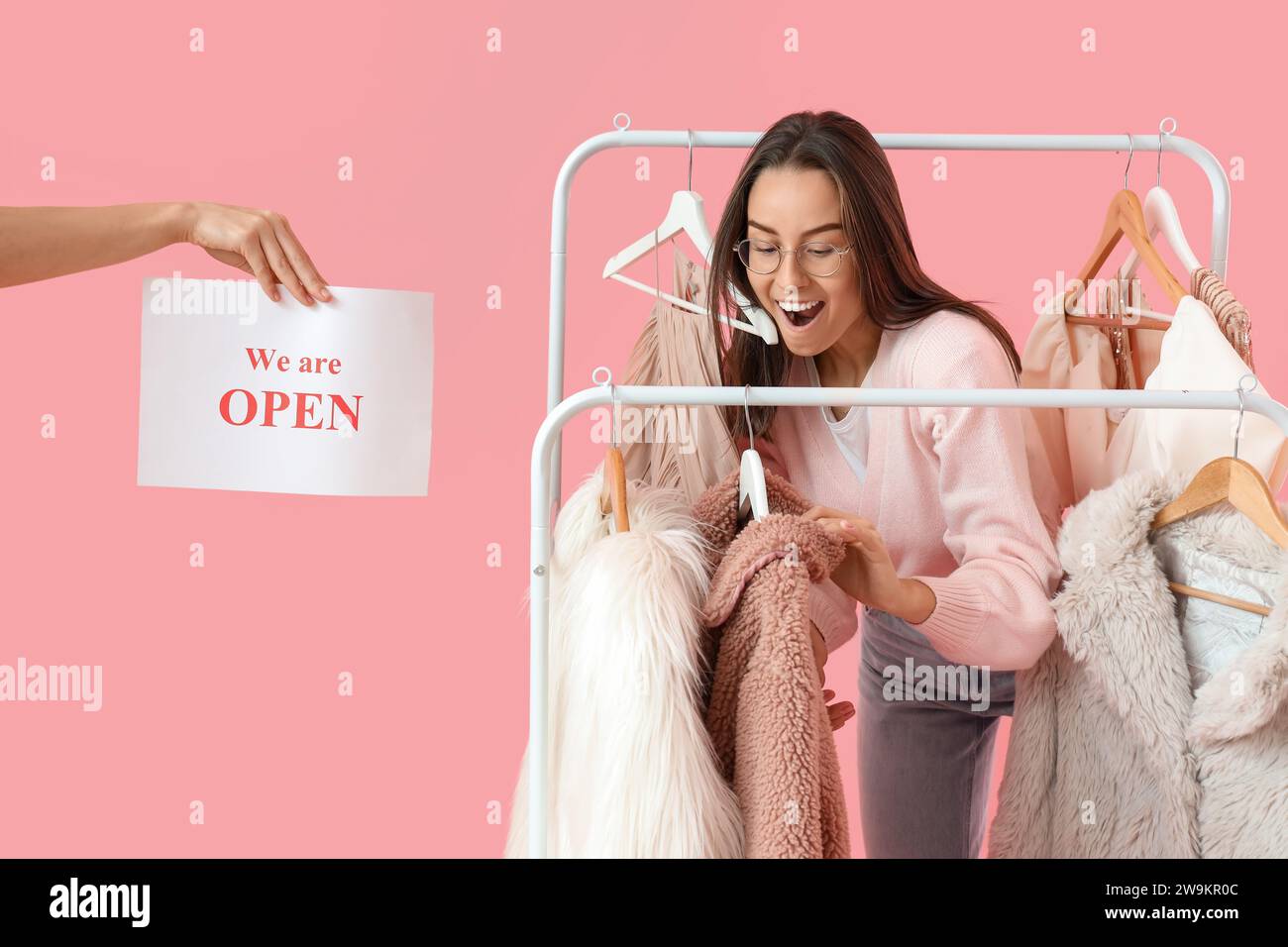 Female seller with clothes racks and OPEN sign on pink background Stock ...
