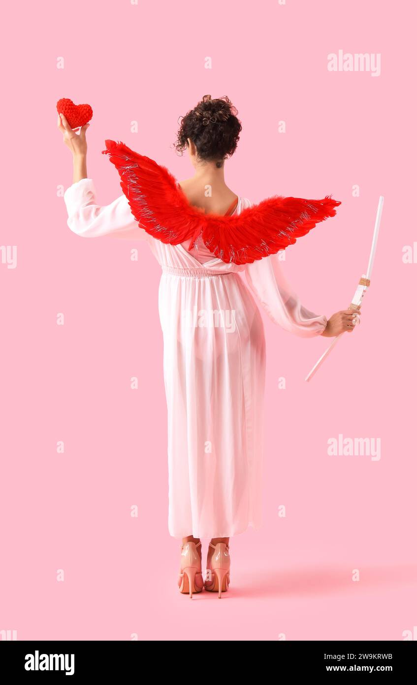 Young woman dressed as Cupid with heart and bow on pink background ...