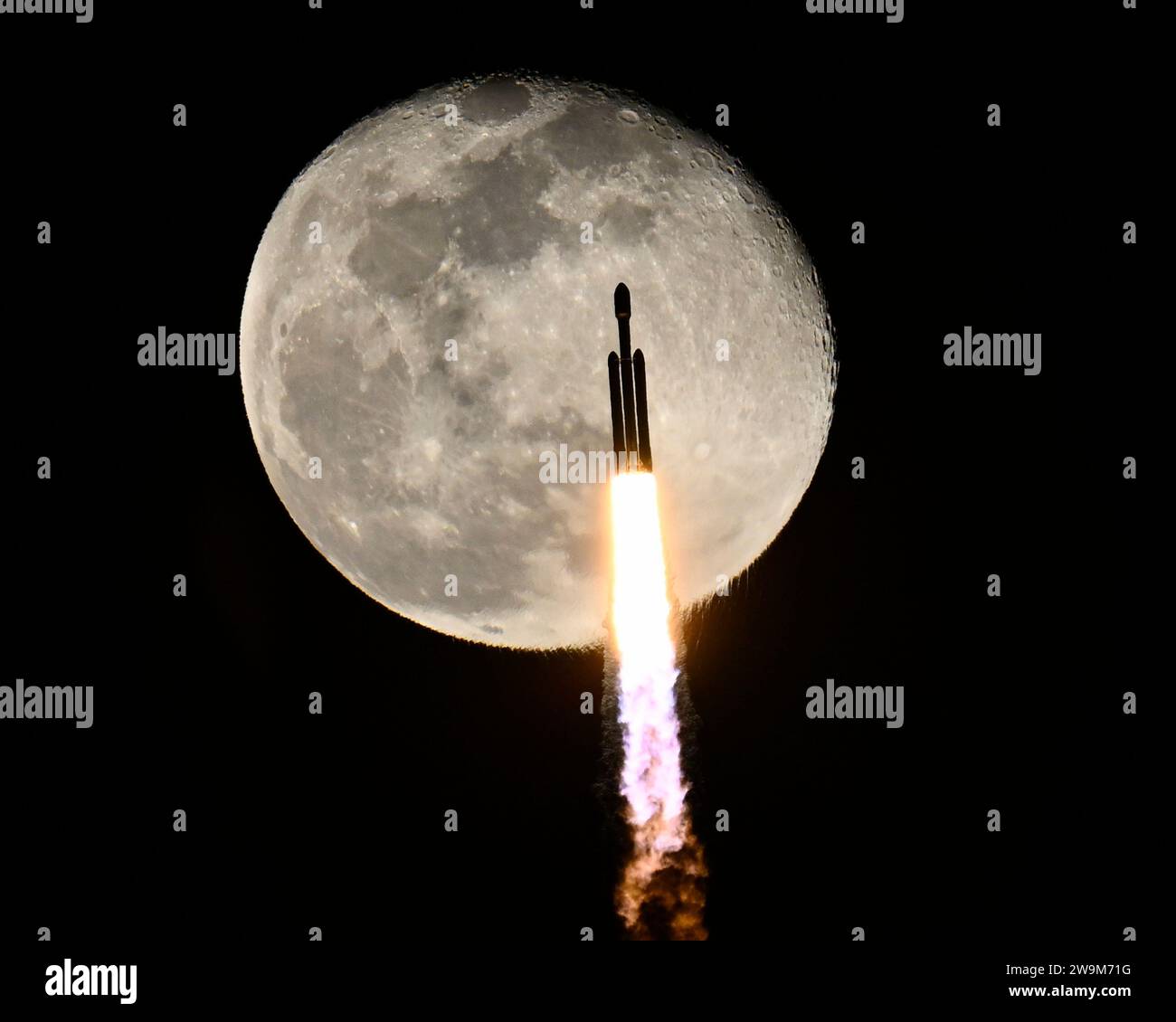 A SpaceX Falcon Heavy rocket transits a near full moon as it launches ...