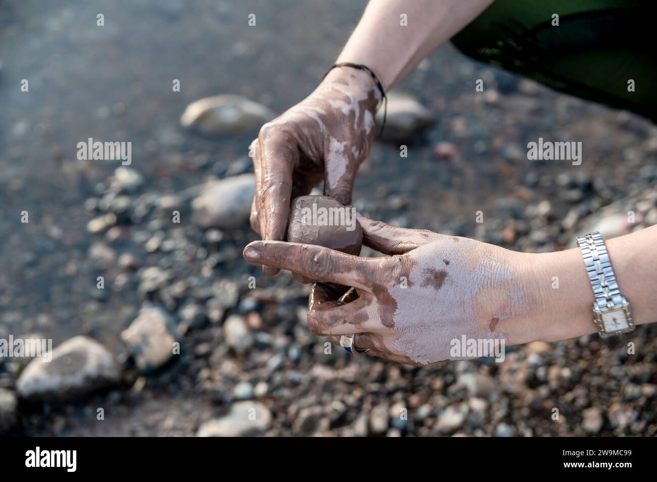 Woman putting mud on hands and face while enjoying outdoors in nature ...