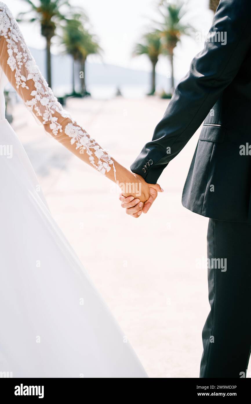 Bride and groom walk holding hands along the promenade. Cropped ...