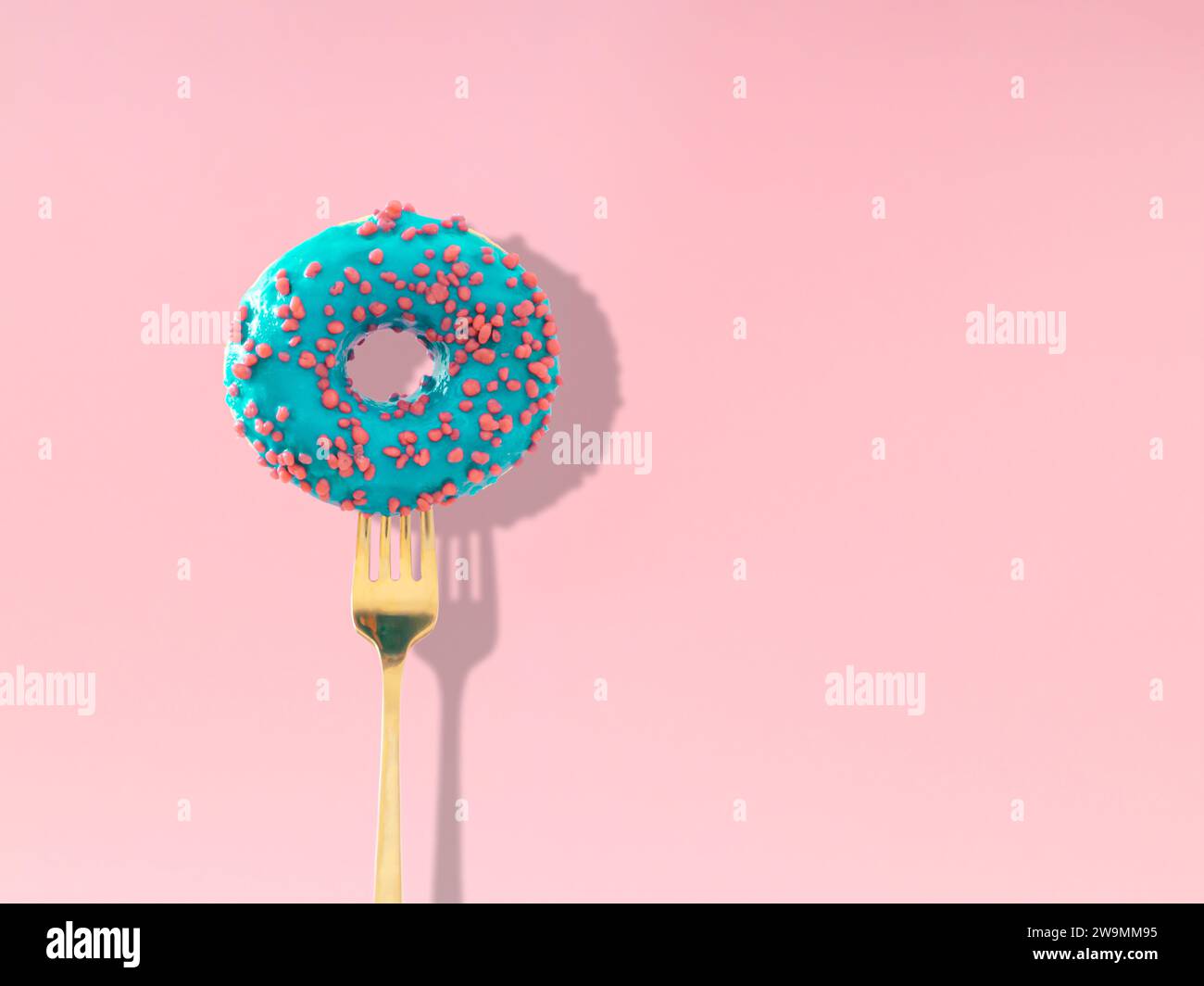 Yummy blue glazed donut pricked on a fork on pastel pink background ...