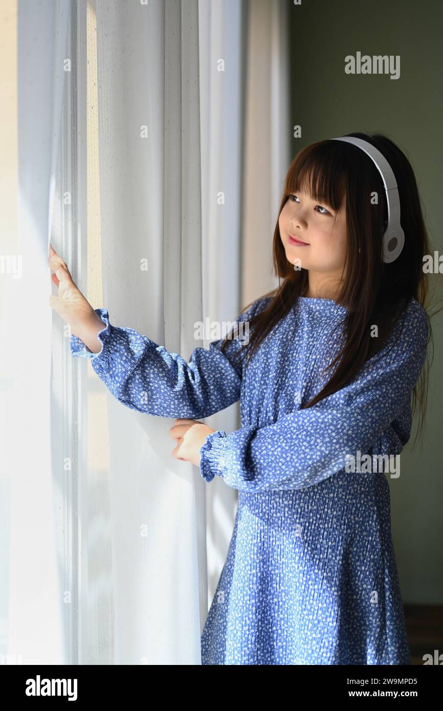 Portrait of pleased Asian child girl listening to music in headphones ...