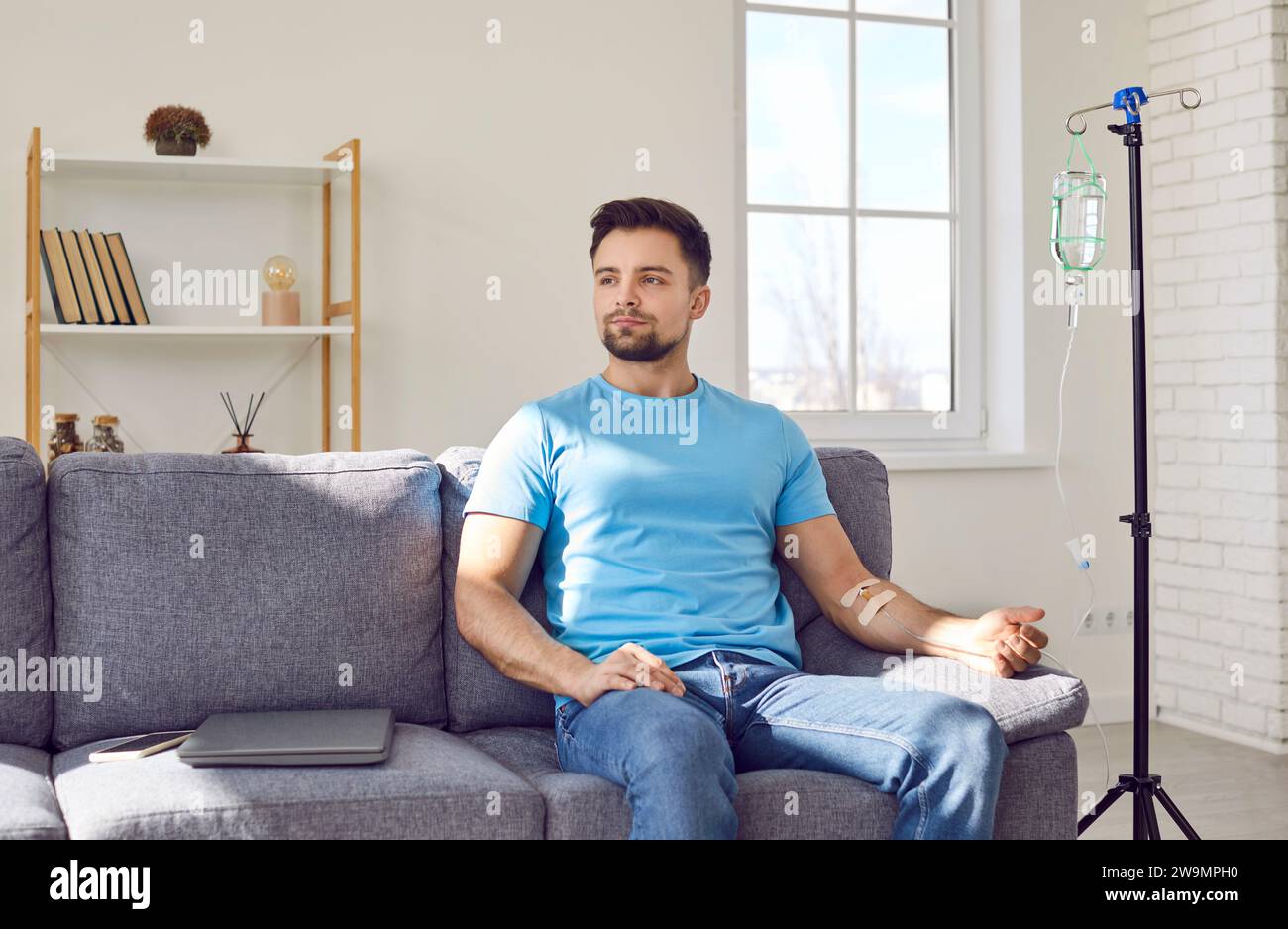 Young man sitting on the sofa at home and getting an intravenous IV ...
