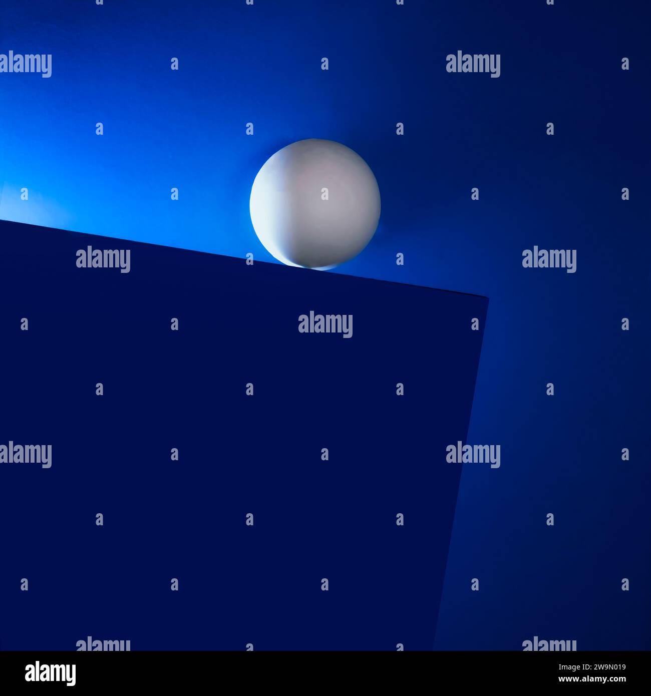 Close-up of a white sphere rolling down the inclined surface of a cube ...