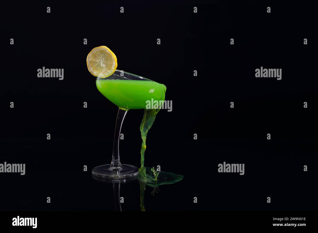 Crooked cocktail glass with drink overflowing onto a table against a ...