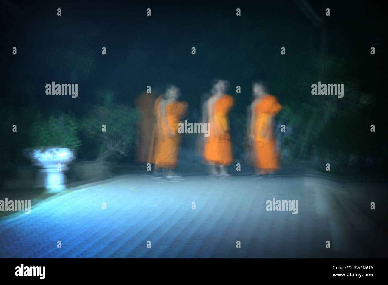 Three Buddhist monks stand in a courtyard at night, lit only by a ...