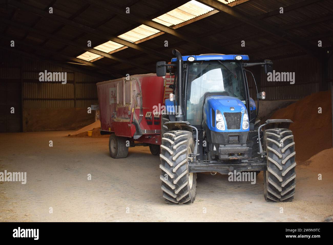 Blue tractor and feeder wagon inside a shed Stock Photo - Alamy