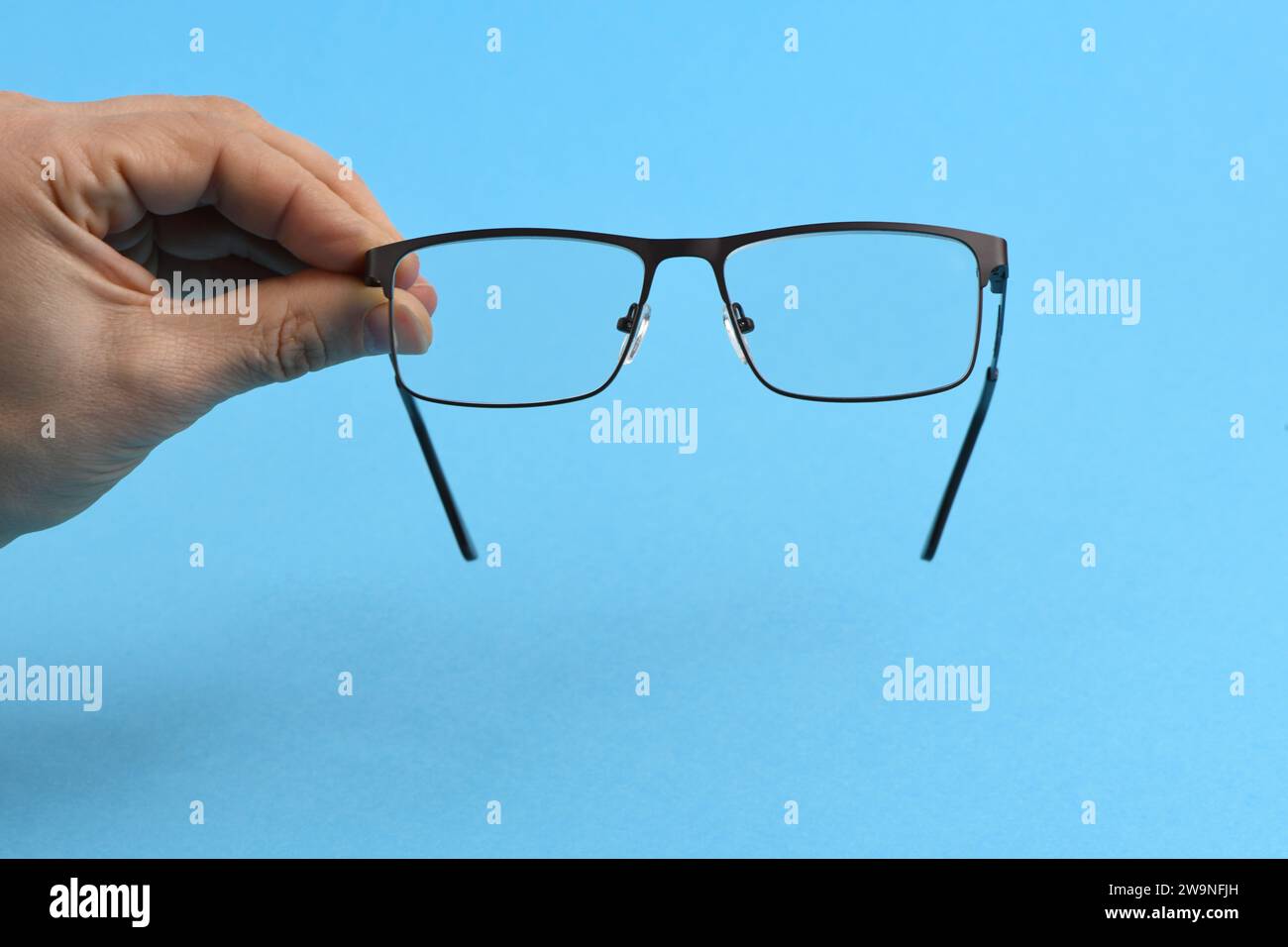 Hand holding plastic black glasses, isolated on blue background. High ...