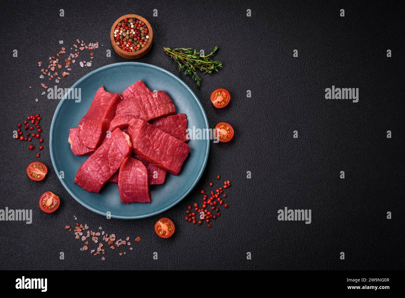 Juicy fresh raw beef meat with salt, spices and herbs on a dark ...