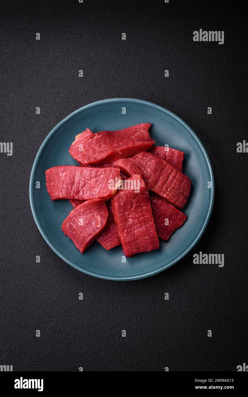 Juicy fresh raw beef meat with salt, spices and herbs on a dark ...
