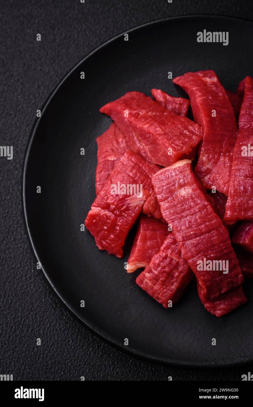 Juicy fresh raw beef meat with salt, spices and herbs on a dark ...