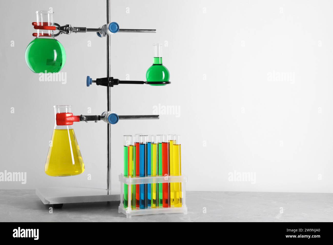 Retort stand and laboratory glassware with liquids on grey table ...