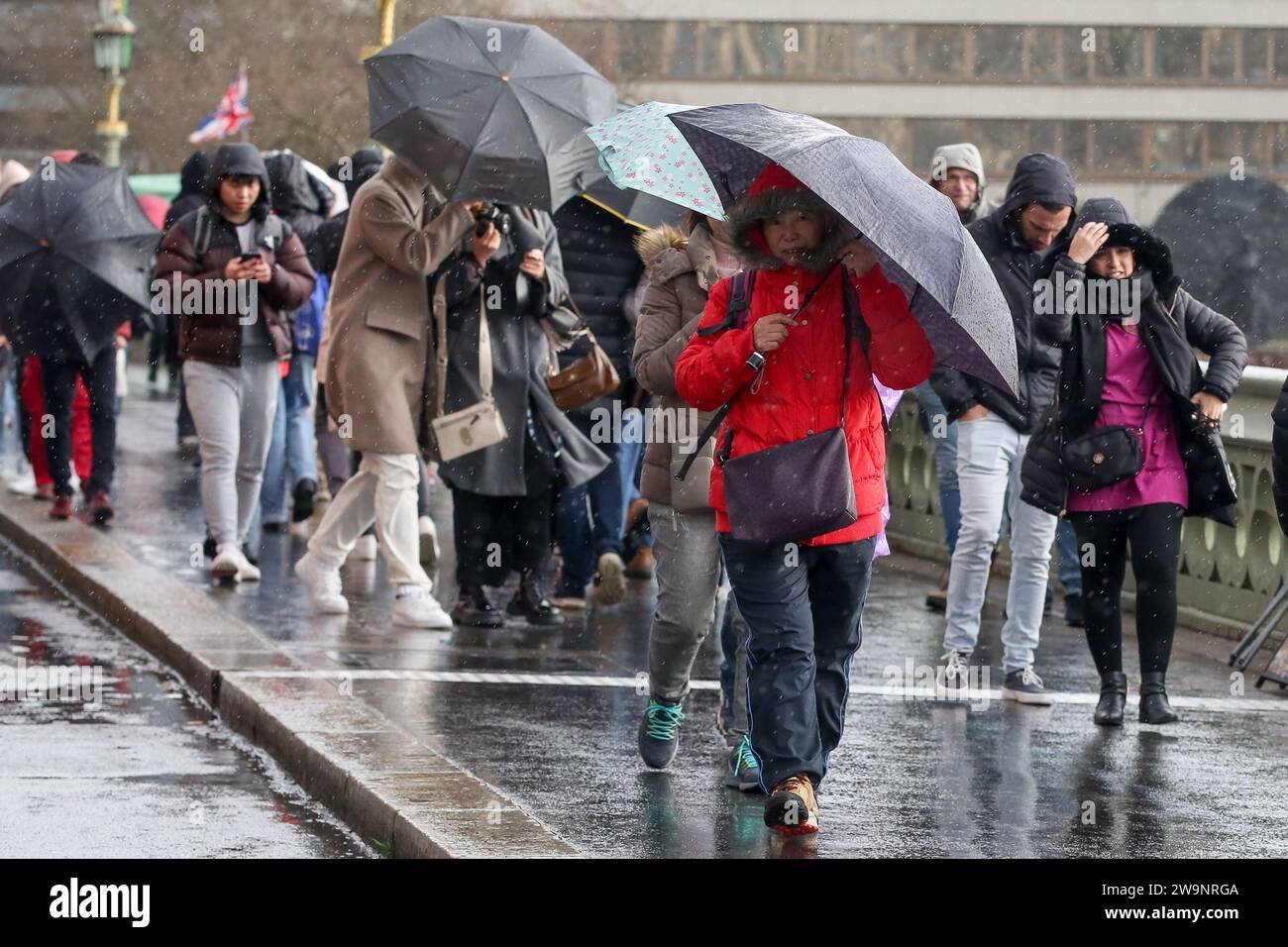 Tourists shelter from wind and rain under umbrellas on Westminster ...