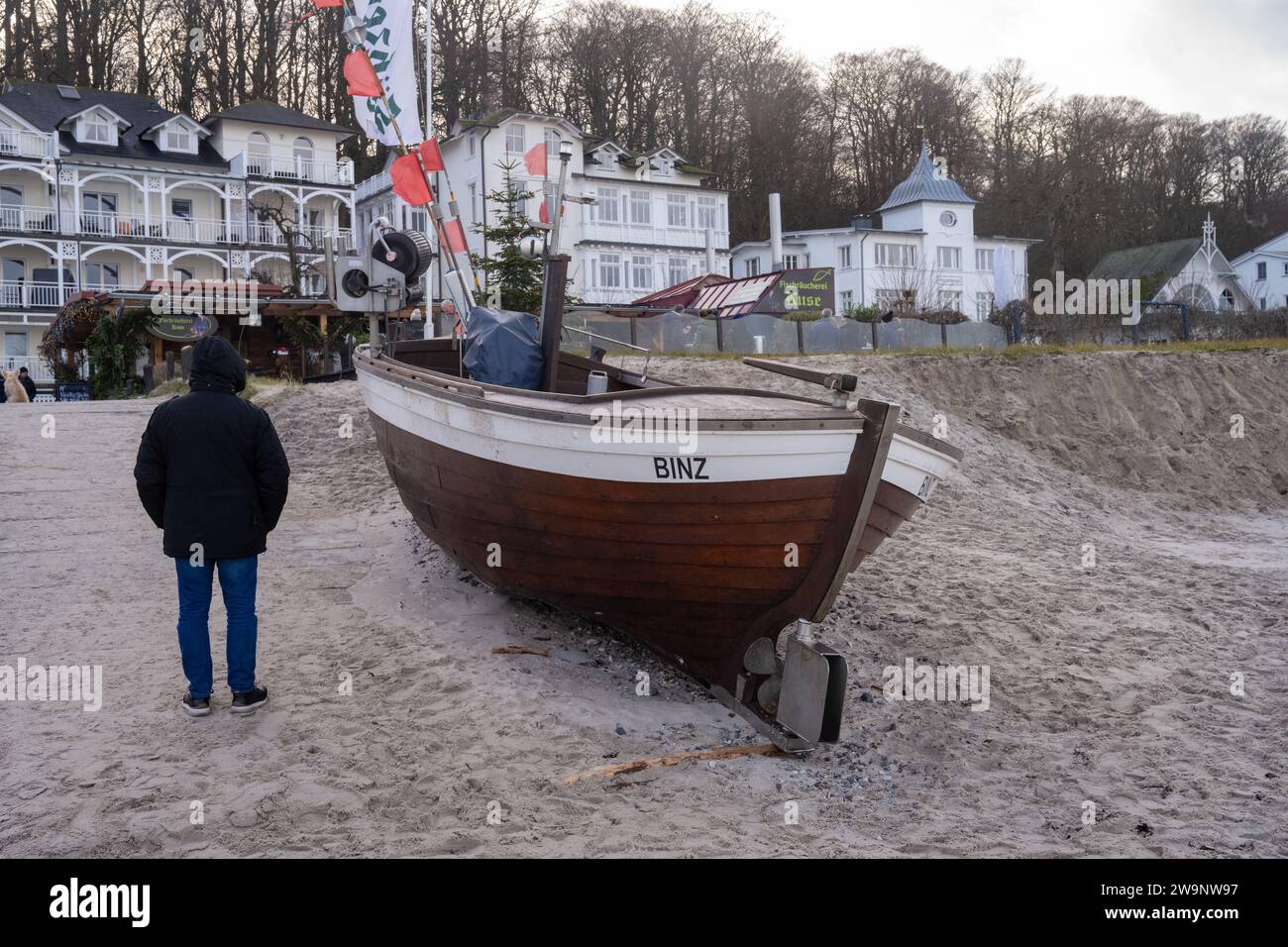 Binz, Germany. 29th Dec, 2023. A walker passes the fishing boat of the ...