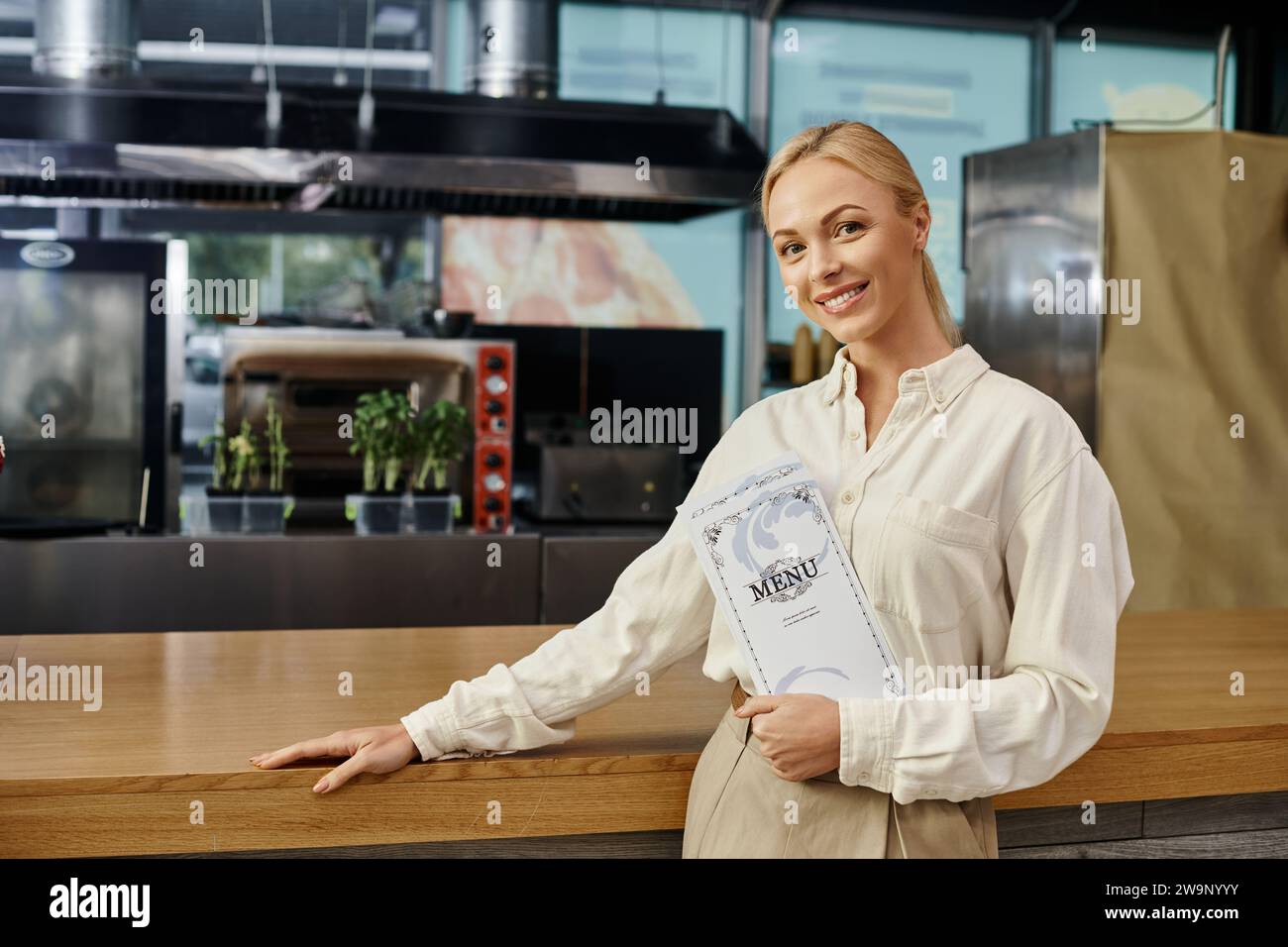 cheerful blonde manager holding menu card and looking at camera near ...