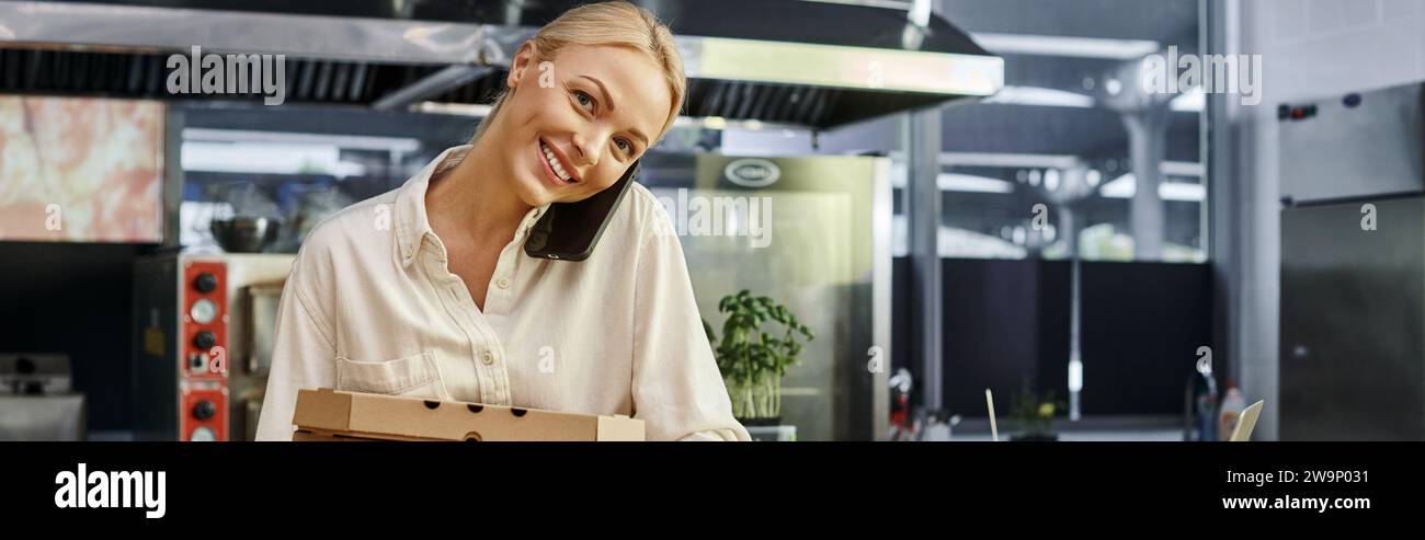 joyful female manager with pizza boxes talking on smartphone and in ...