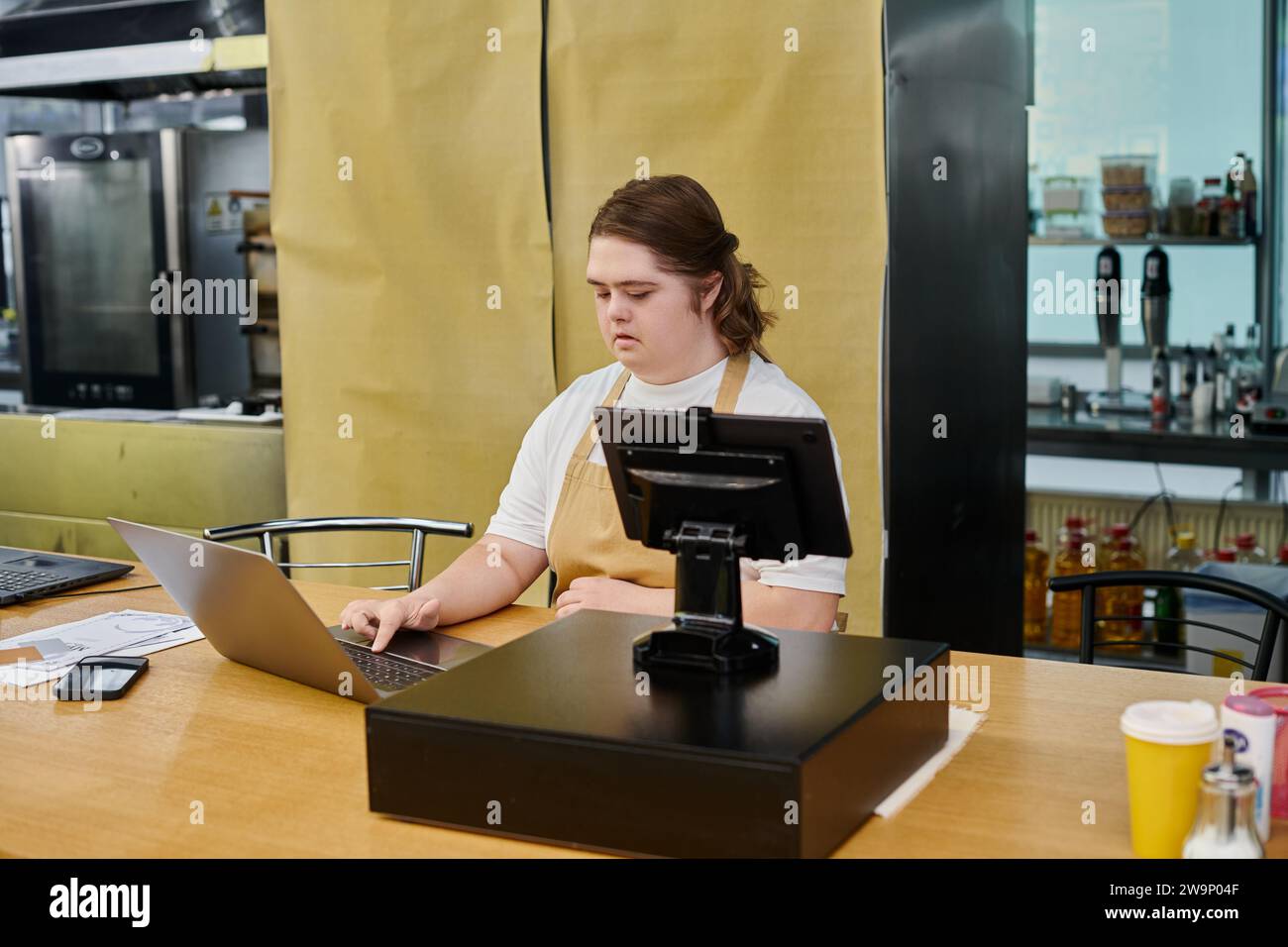 young female employee with down syndrome working with laptop and cash ...