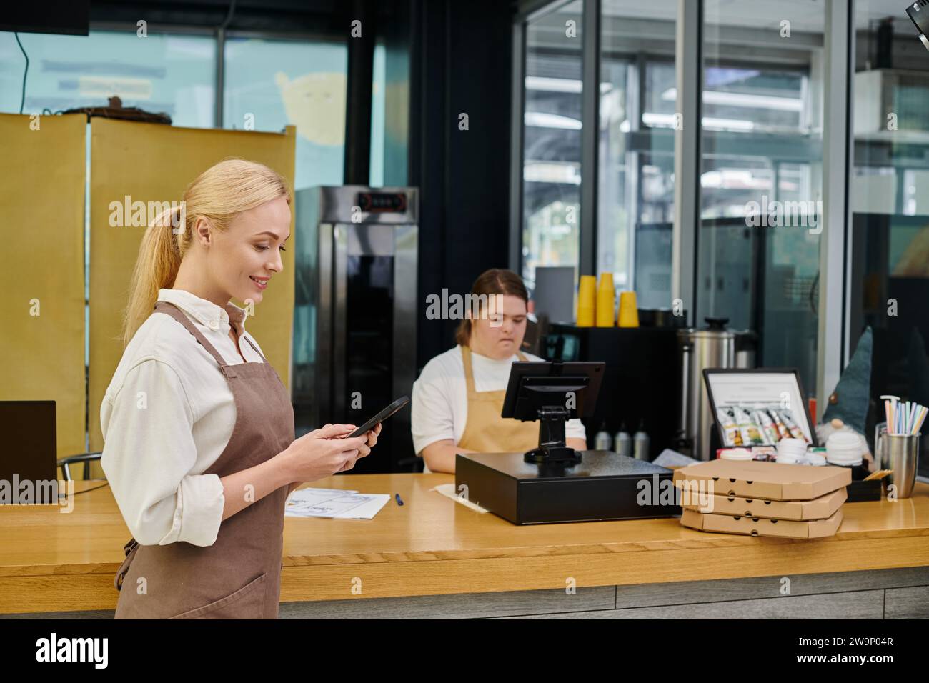 happy cafe manager messaging on smartphone near female employee with ...