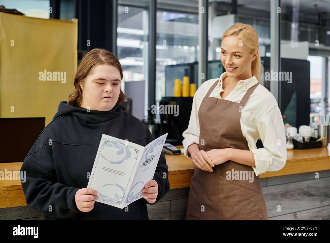 young woman with mental disorder looking at menu card near smiling administrator in modern cafe ...