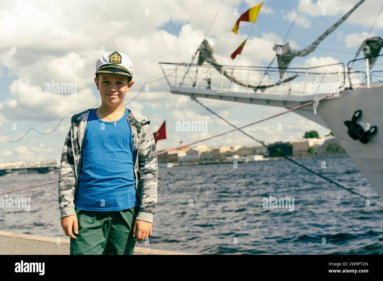 Adorable school-age boy wearing a captain's cap standing near the ship ...
