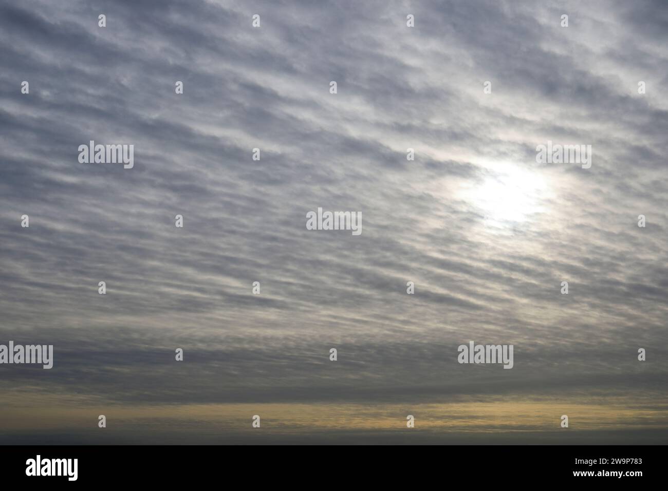 A cloudy winter sky with diagonal lines of cloud and the sun behind ...