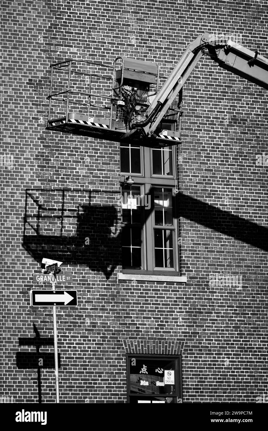 Hydraulic work platform casts a shadow on the side of a brick building ...