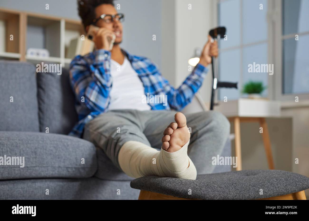 Man talking on phone while sitting on couch, with his injured foot ...