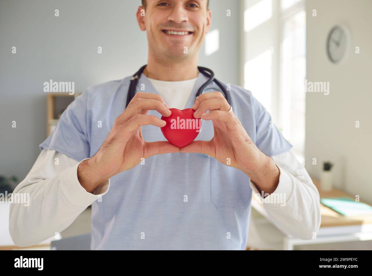Male smiling man doctor cardiologist in blue uniform holding red heart ...