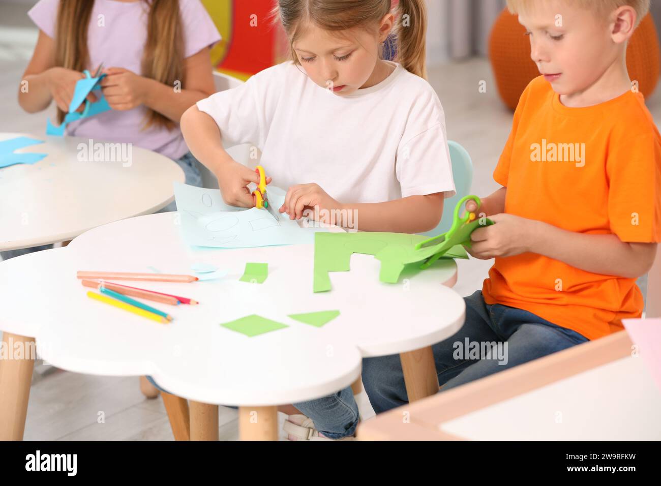 Cute little children cutting color paper with scissors at desks in ...
