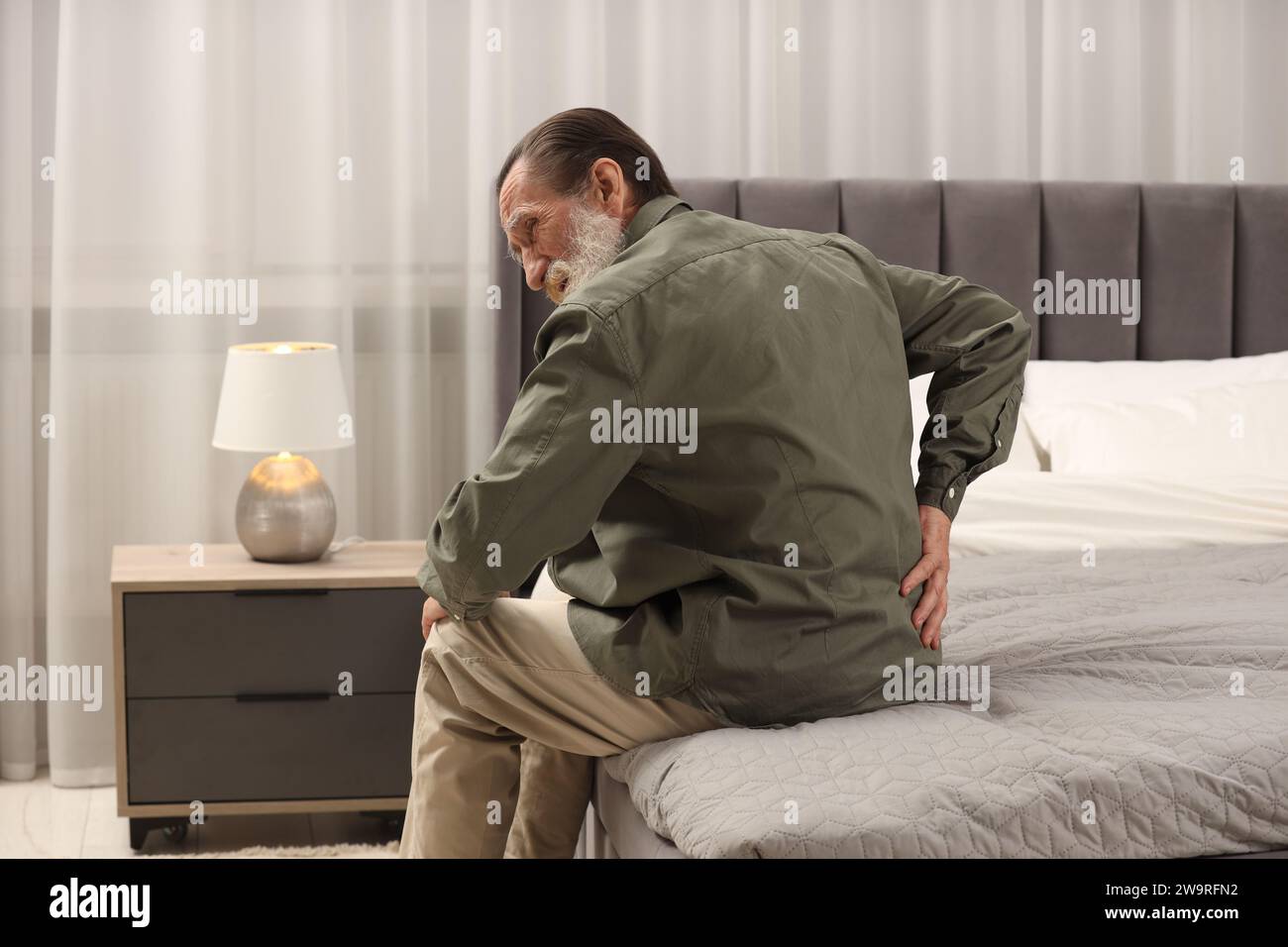 Senior man suffering from back pain on bed at home. Rheumatism symptom ...