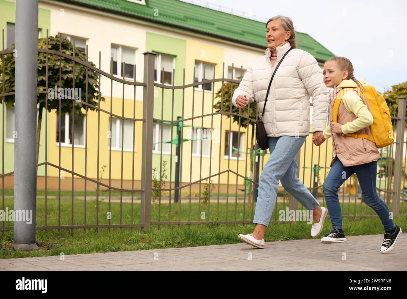 Being late for school. Senior woman and her granddaughter with backpack ...